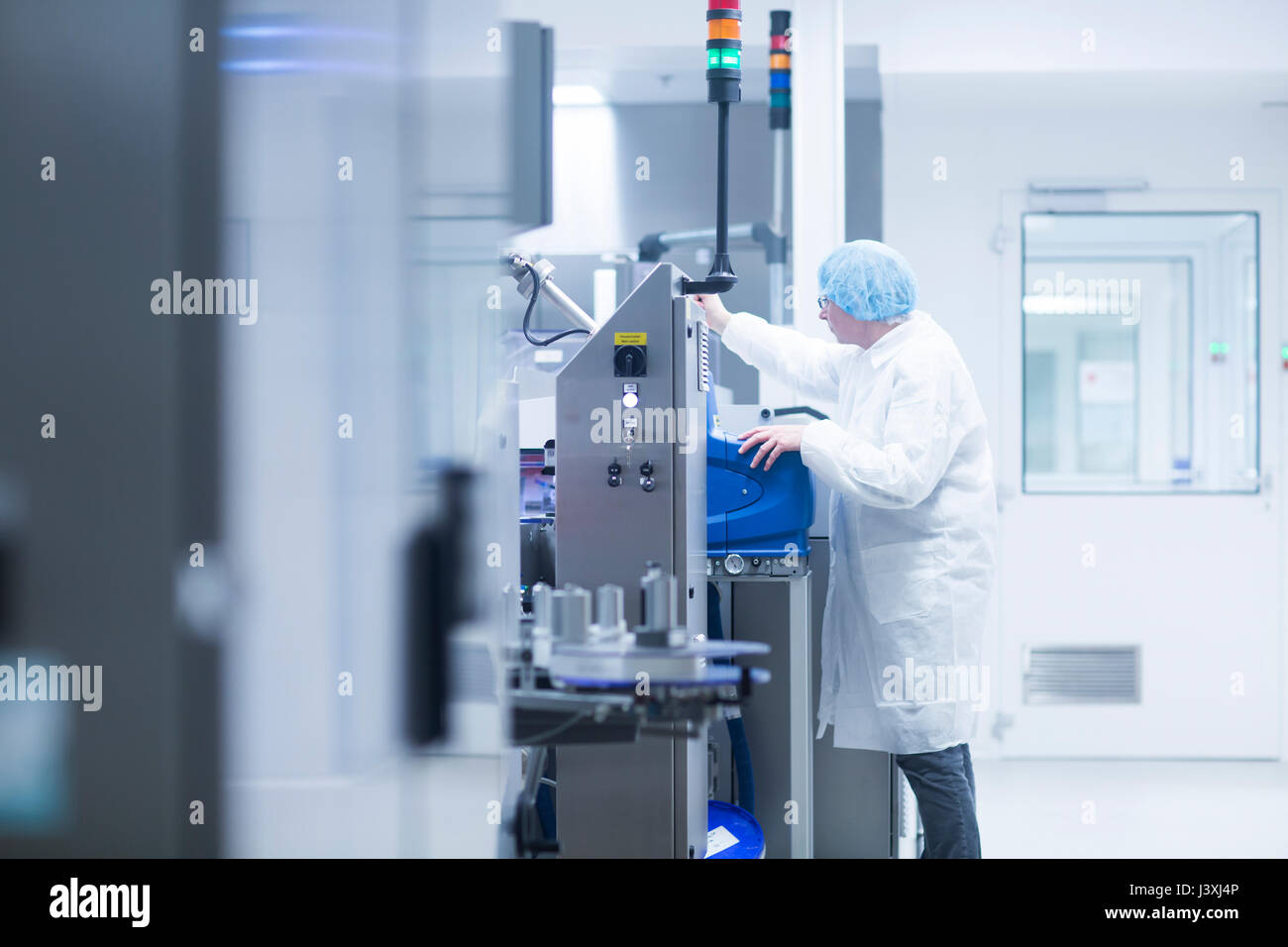 Worker operating machinery on production line in pharmaceutical plant ...