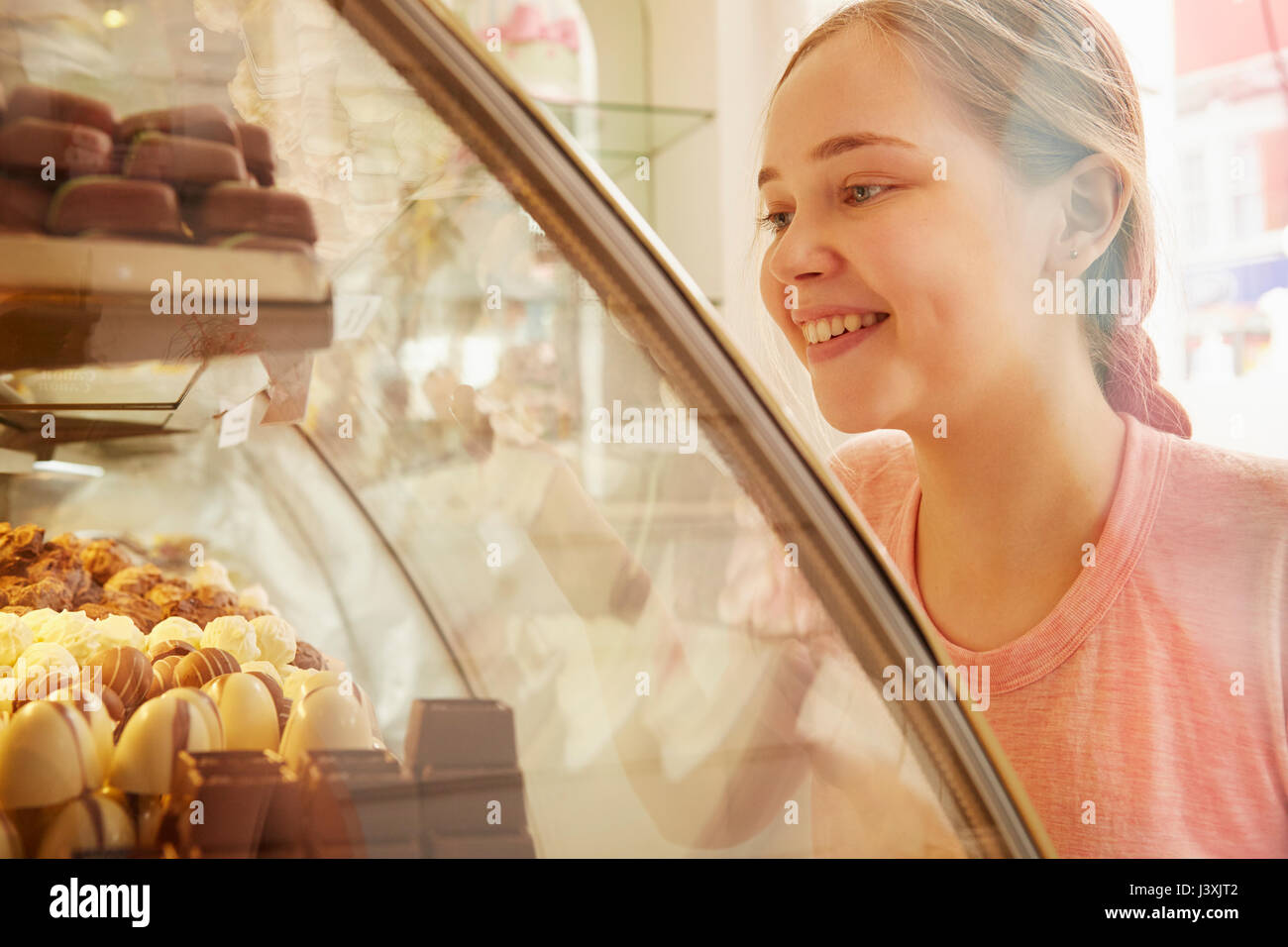 Girl in bakery looking at cakes in display cabinet smiling Stock Photo ...