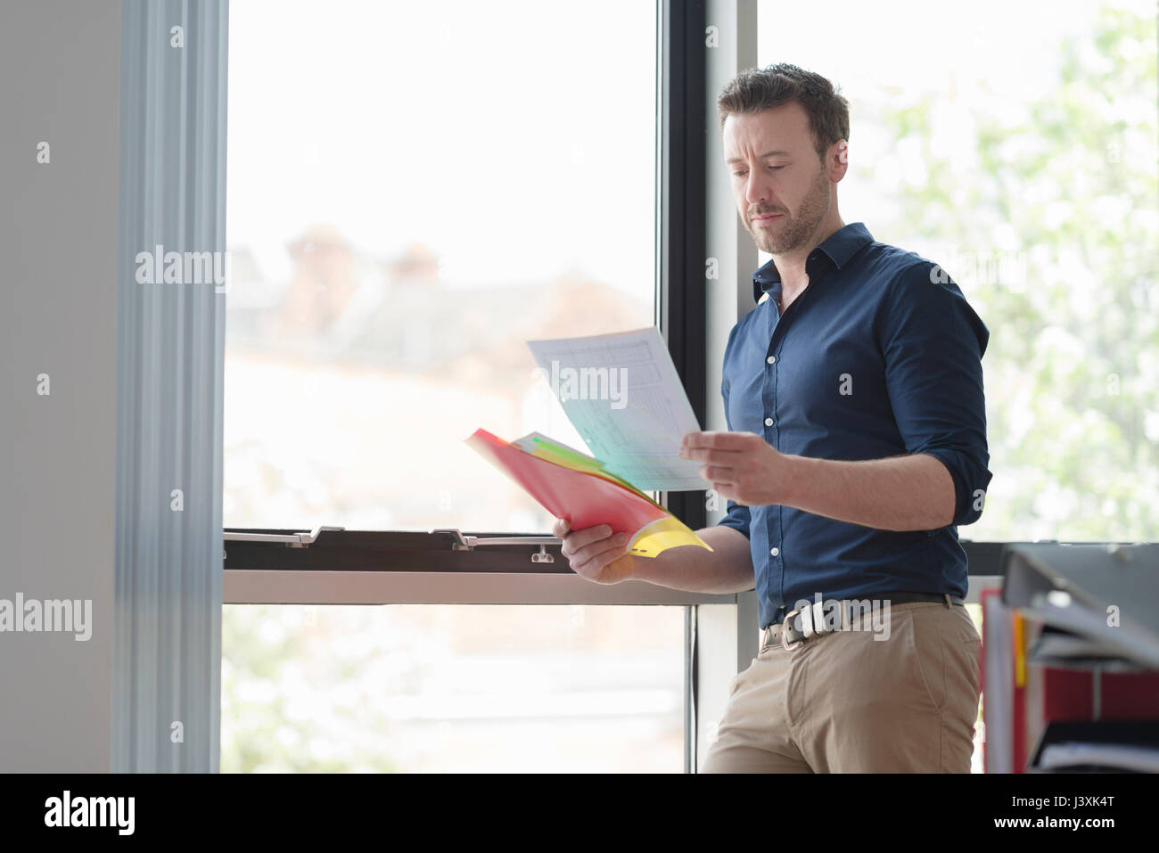 Man contemplating and reading papers by office window Stock Photo - Alamy