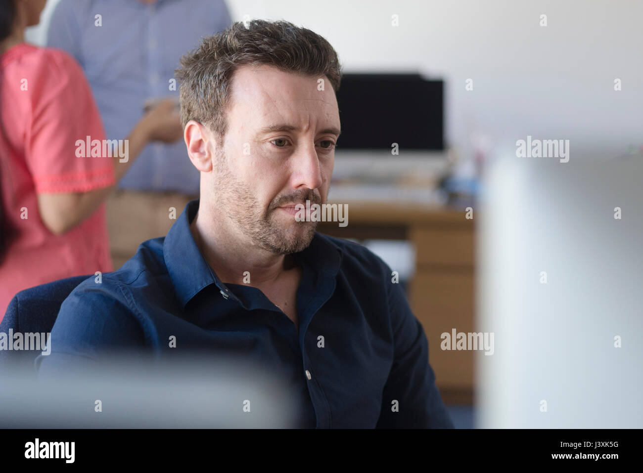 Man working at computer on office desk, colleagues on coffee break in ...