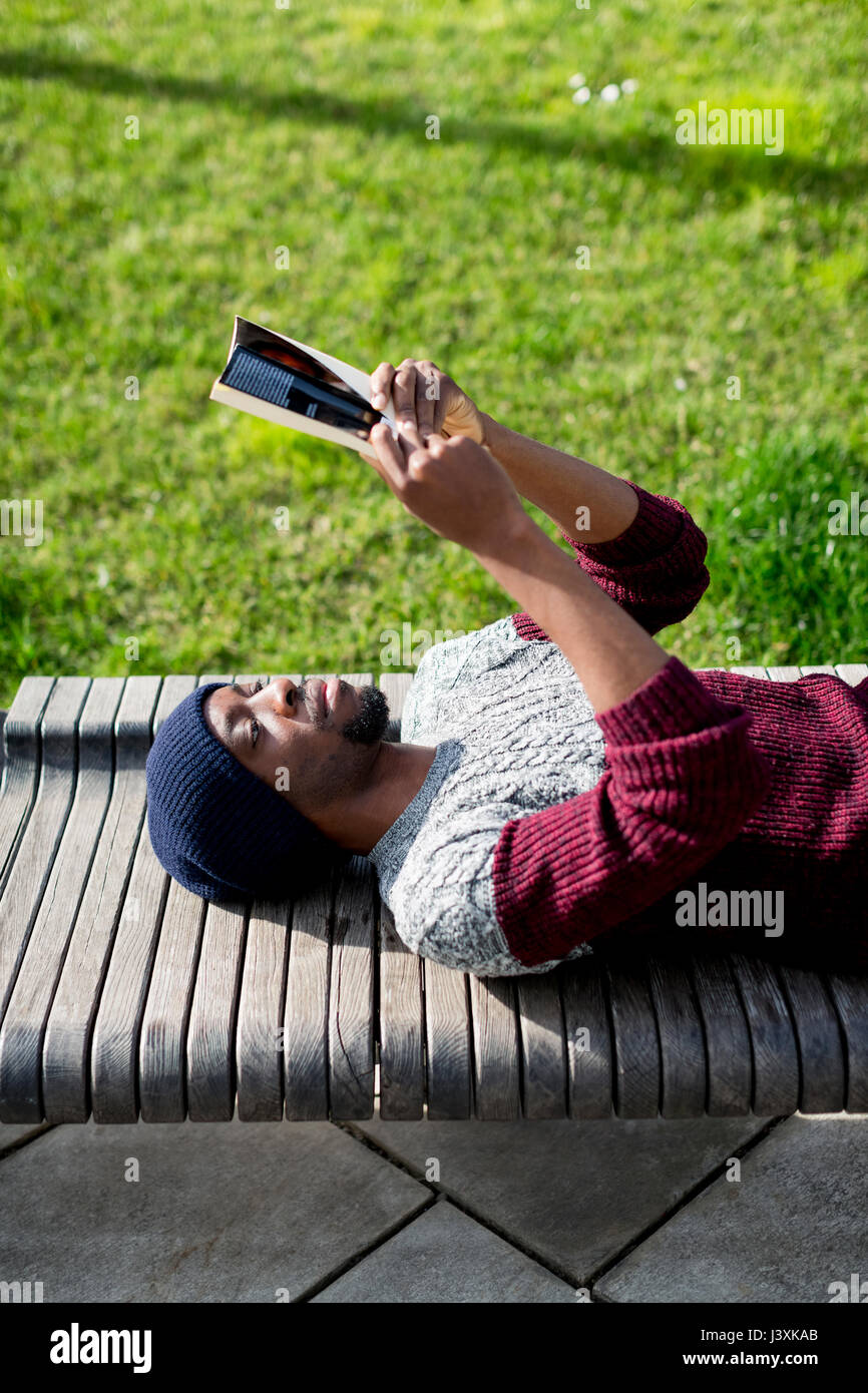 Man lying on bench, reading book Stock Photo - Alamy