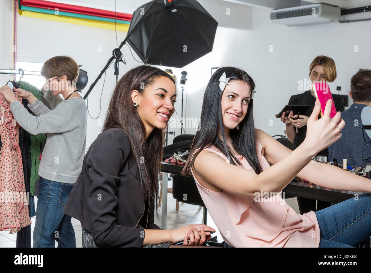 Two fashion models taking smartphone selfie in photographers studio ...