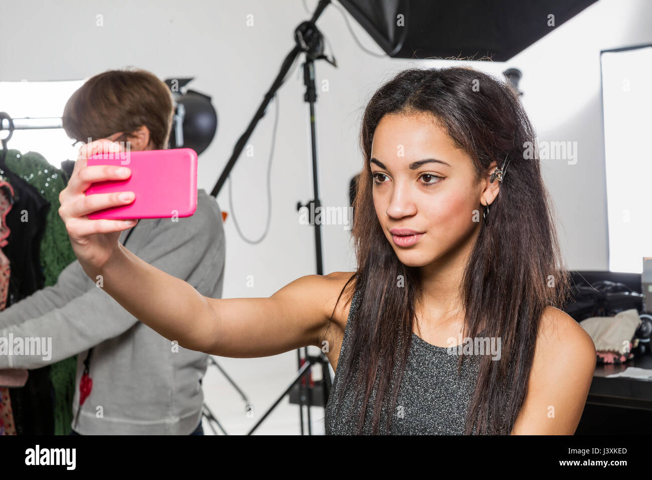 Young female fashion model taking smartphone selfie in photographers ...