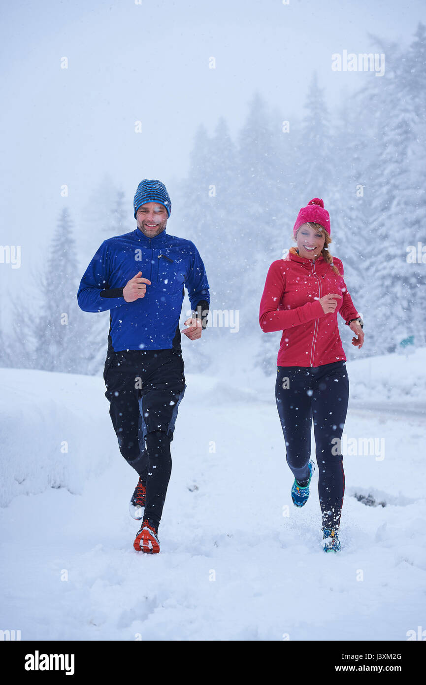 Female and male runners running in falling snow, Gstaad, Switzerland ...
