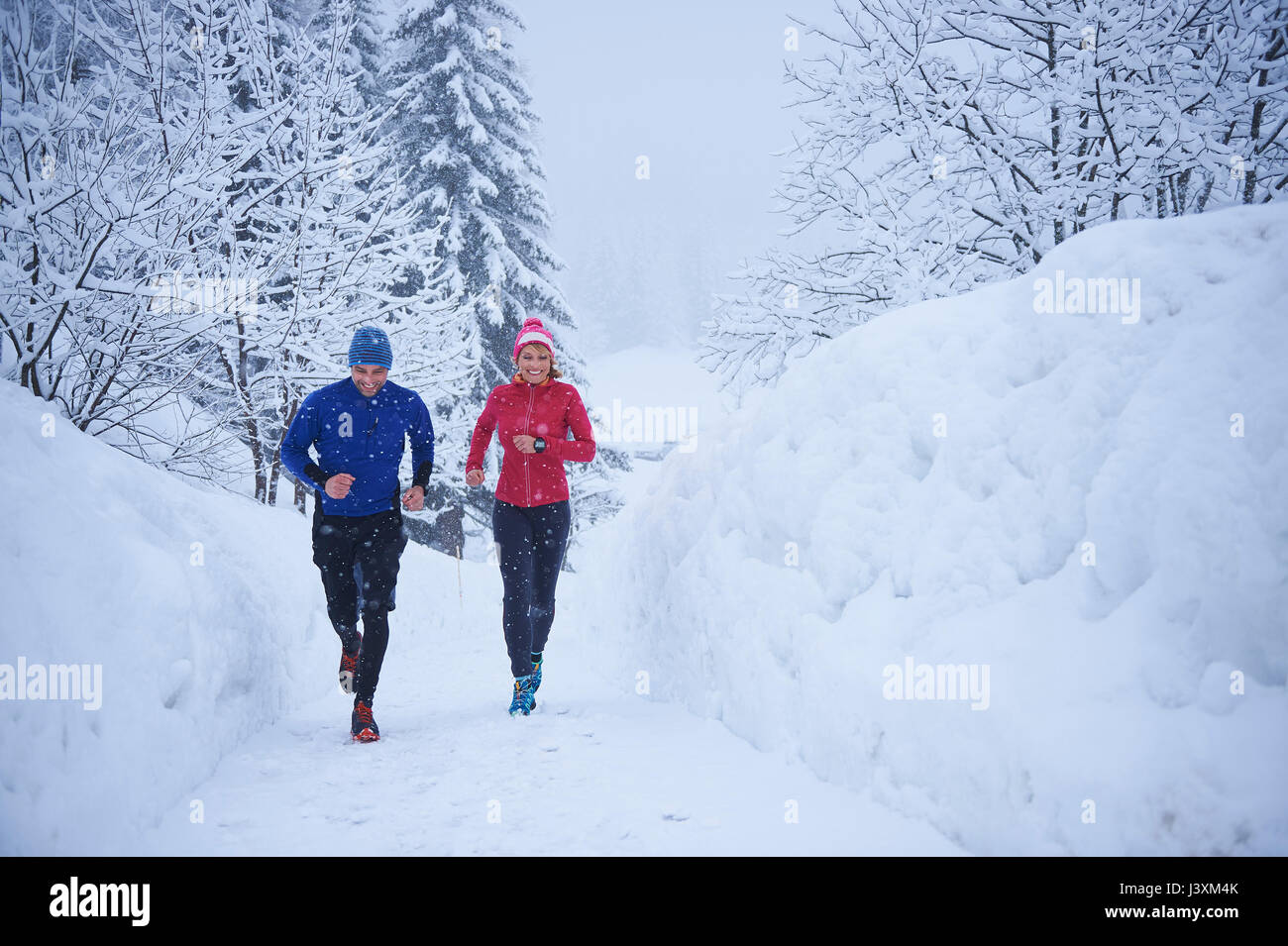 Female and male runners running in falling snow, Gstaad, Switzerland ...