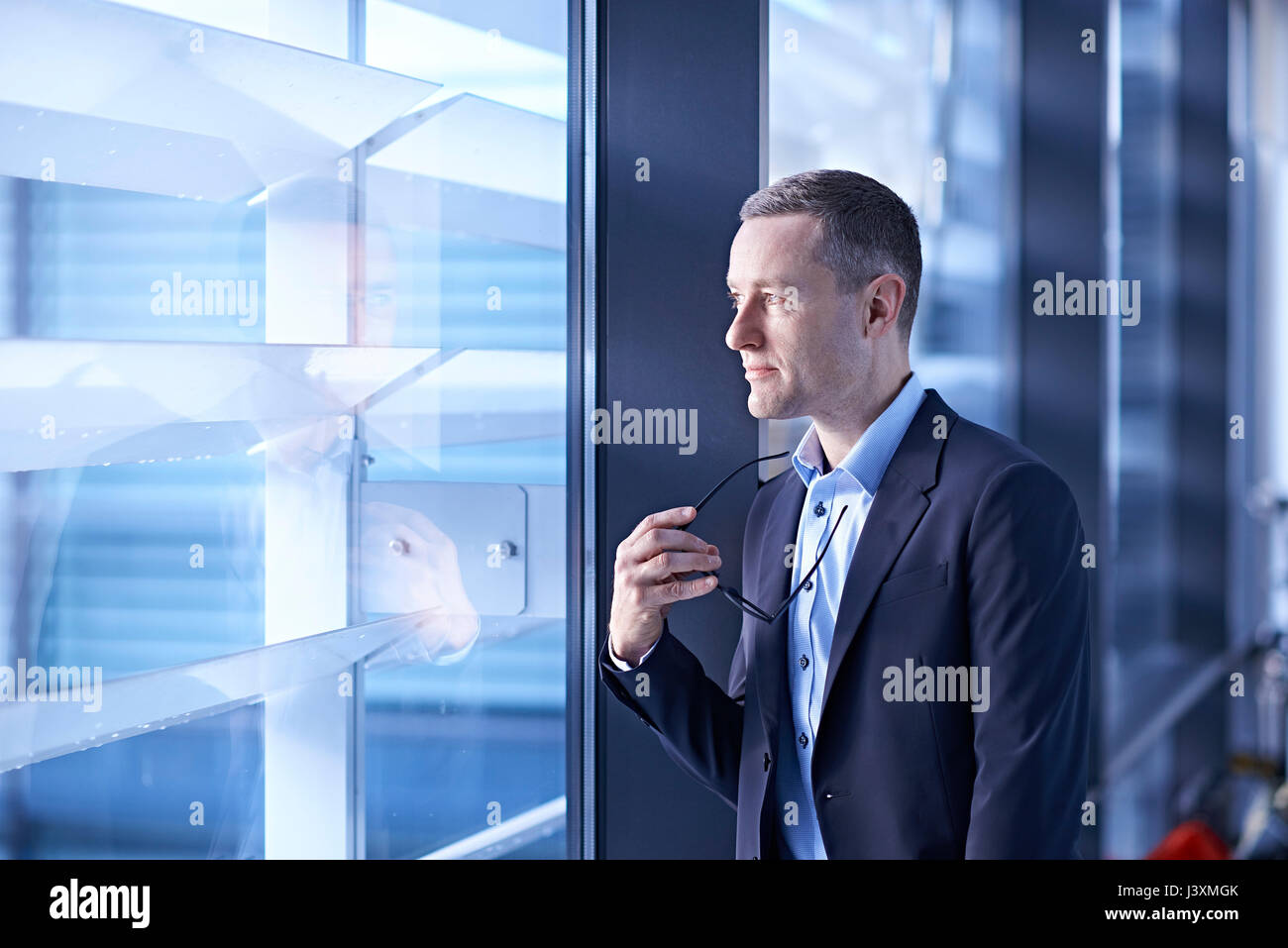 Businessman holding eyeglasses and looking through office window Stock ...