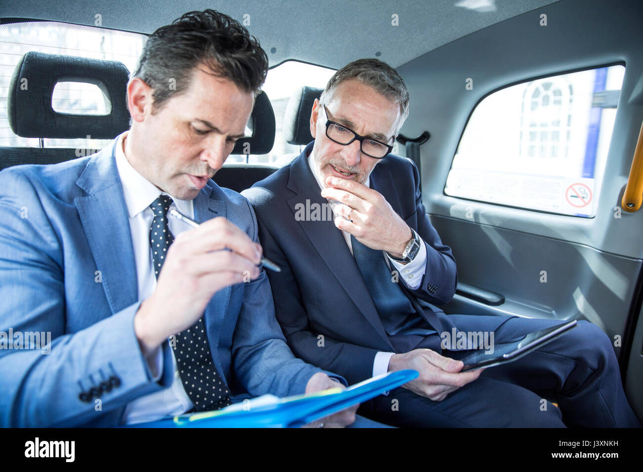 Two businessmen looking at paperwork in taxi cab Stock Photo - Alamy