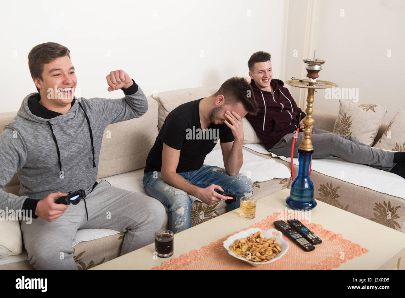 Three Young Gamers Sitting Together On Sofa And Playing Video Games At ...