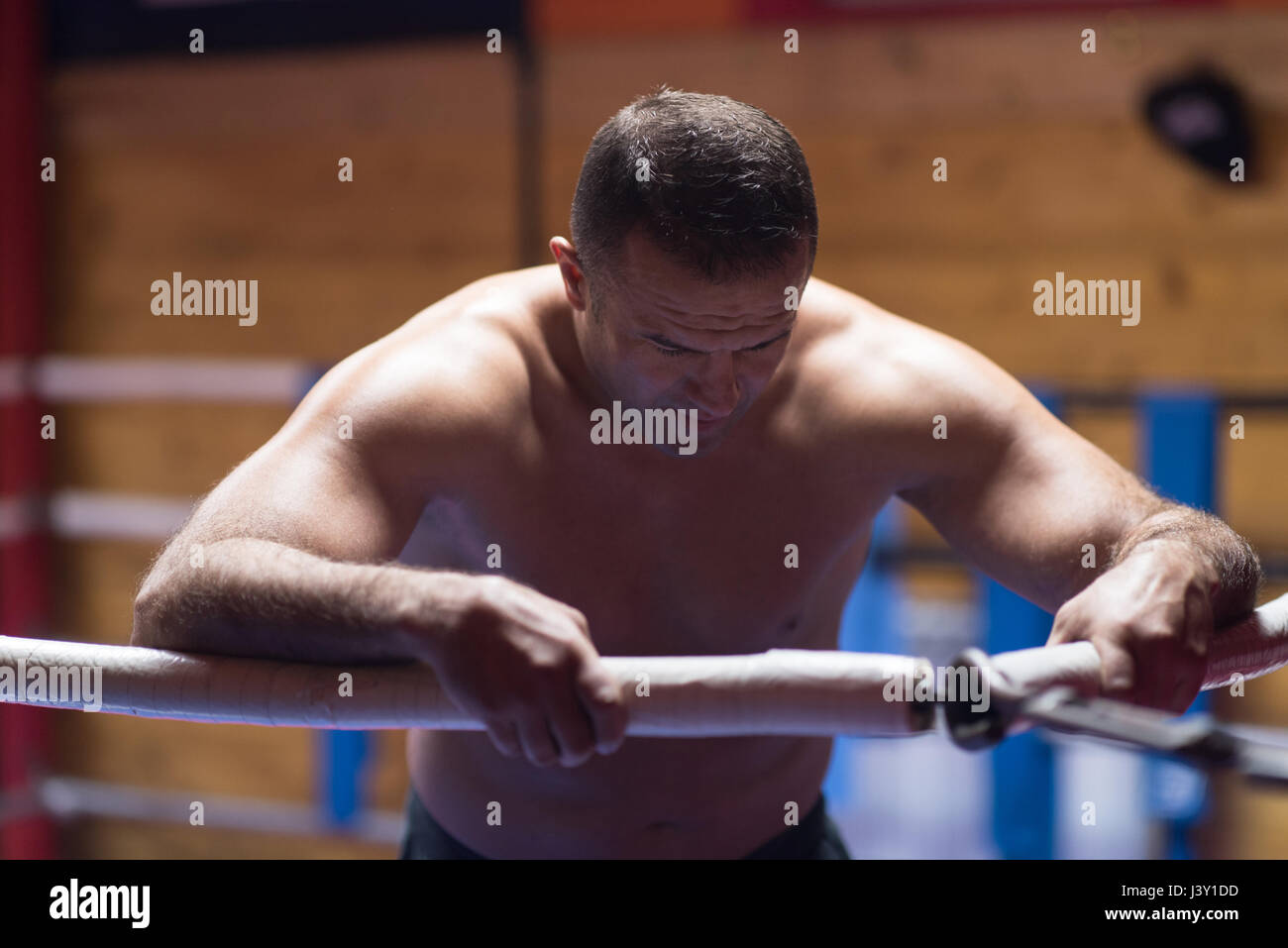 muscular professional kick boxer resting on the ropes in the corner of ...