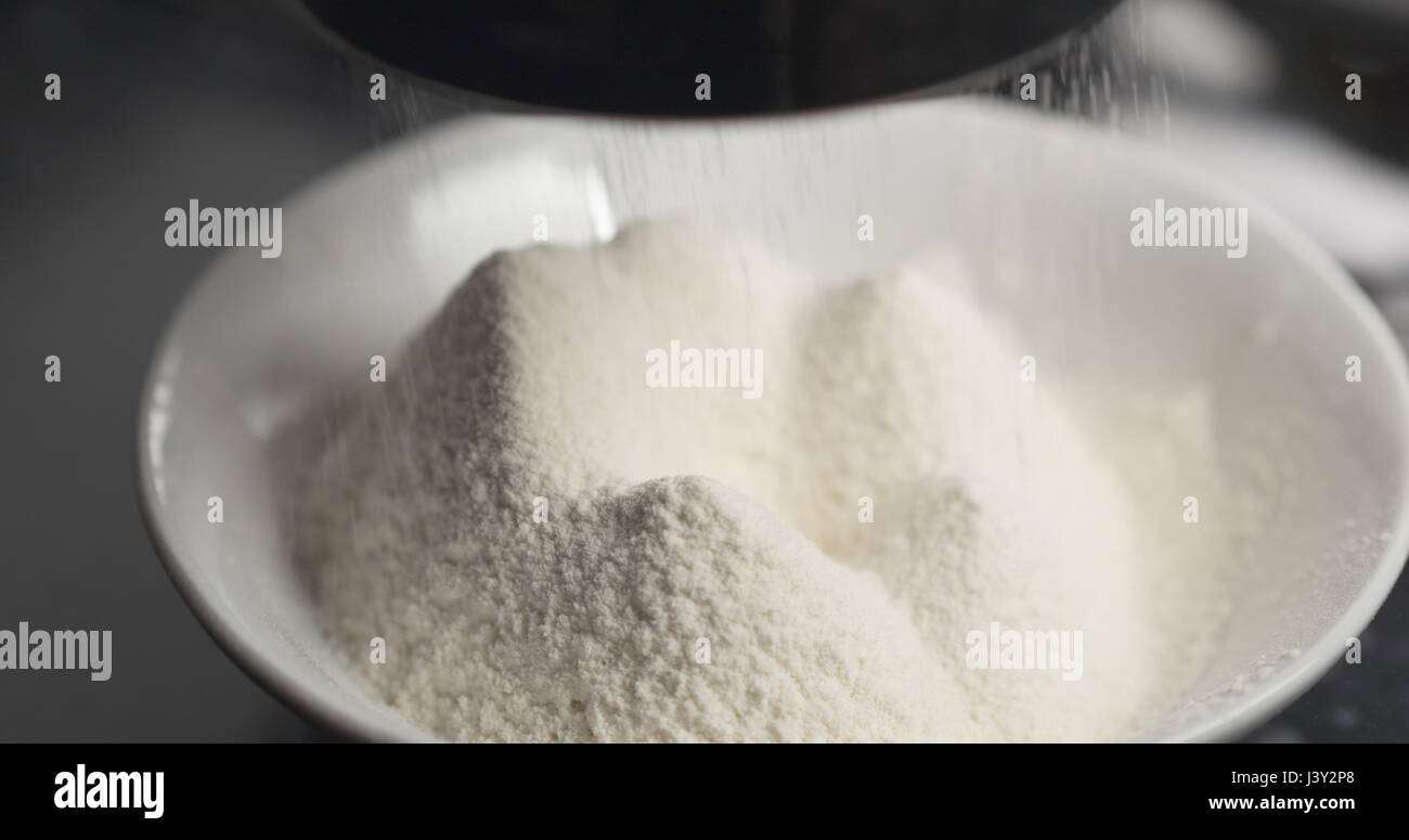 Handheld shot of sieving flour with mug sieve on plate closeup Stock ...