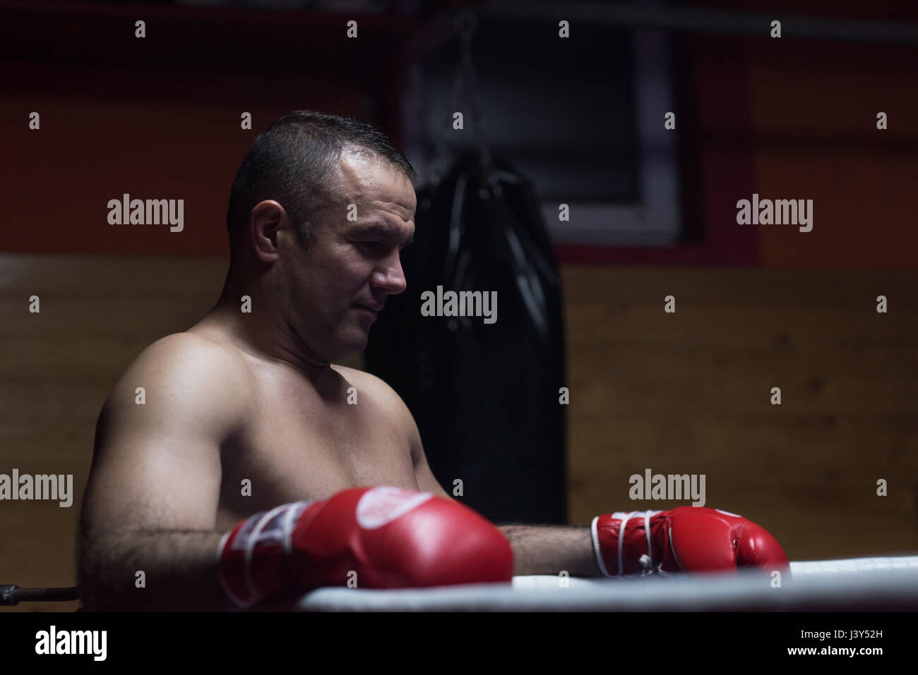 muscular professional kick boxer resting on the ropes in the corner of ...