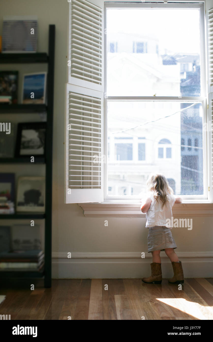 Rear view of female toddler looking through apartment window Stock ...