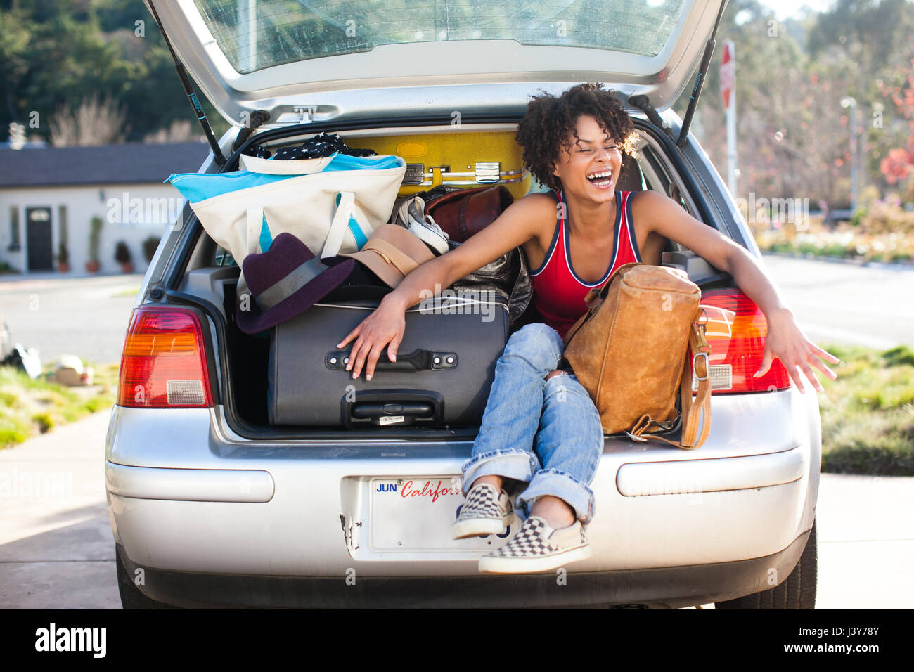 Woman sitting in car boot with luggage laughing Stock Photo - Alamy