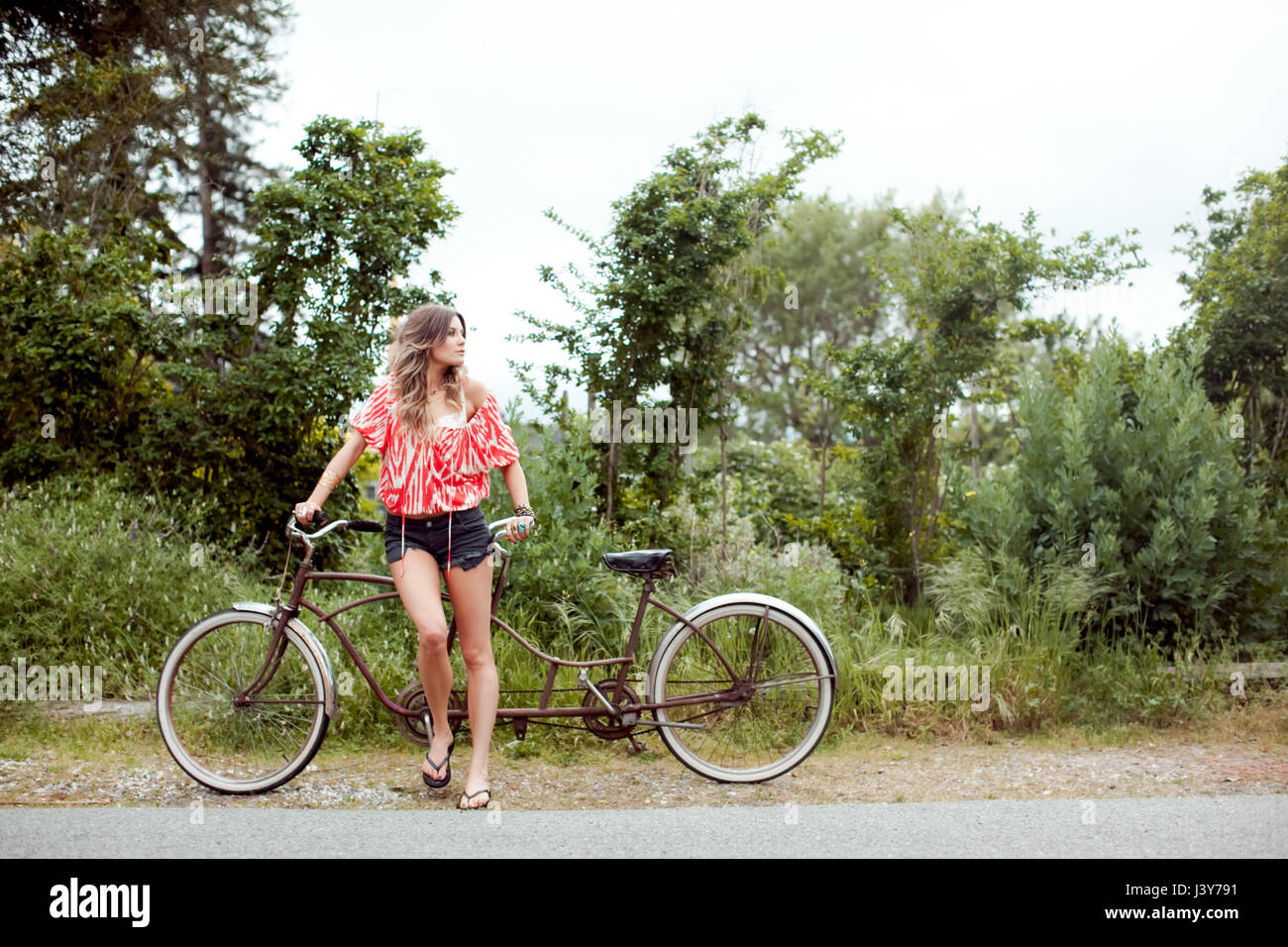 Young woman with tandem bicycle looking over her shoulder on rural road ...
