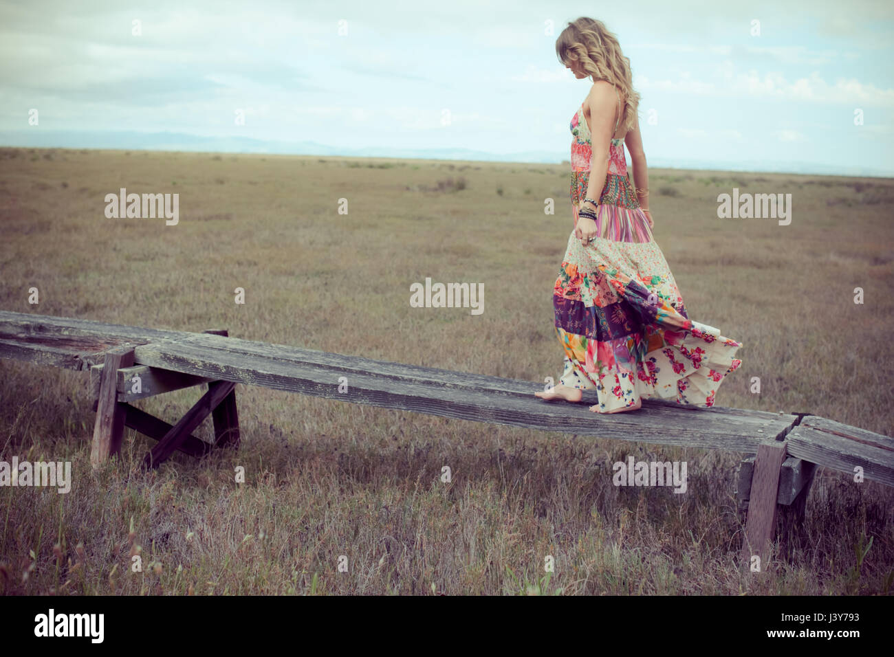 Young woman in boho maxi dress walking on elevated wooden walkway in ...