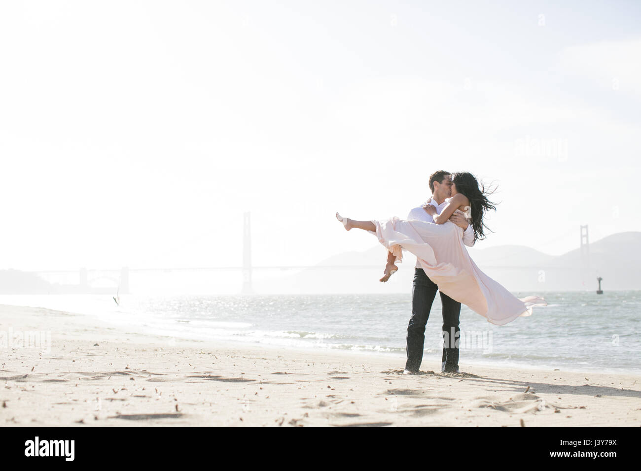 Romantic man carrying girlfriend in arms on beach, San Francisco Bay ...
