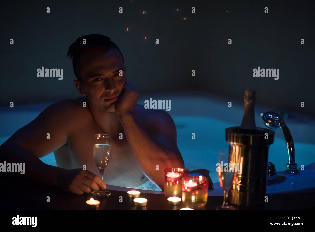 young handsome man enjoys relaxing in the jacuzzi with candles and ...