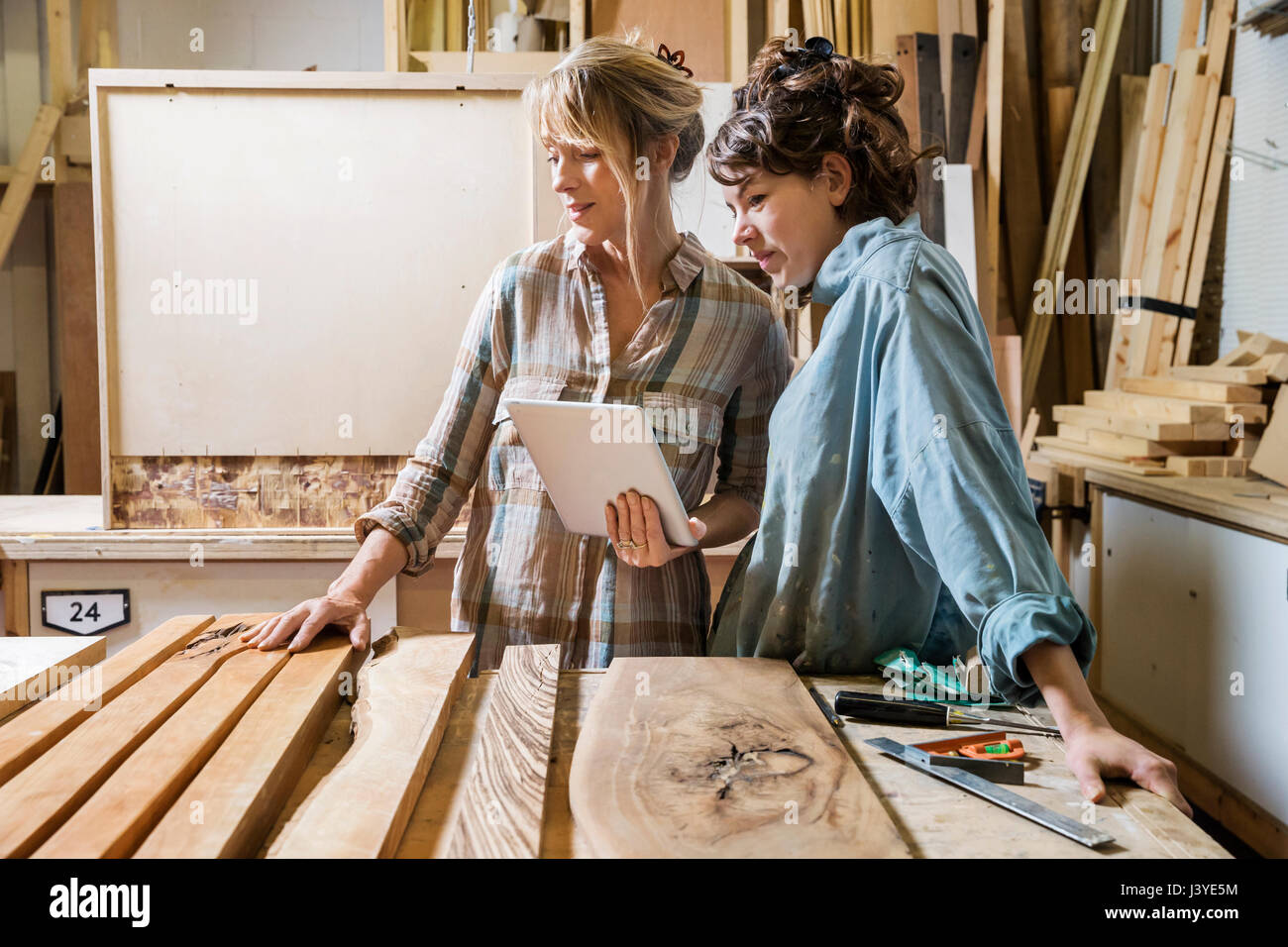 Two women choosing wood from a selection in a workshop, consulting on a ...
