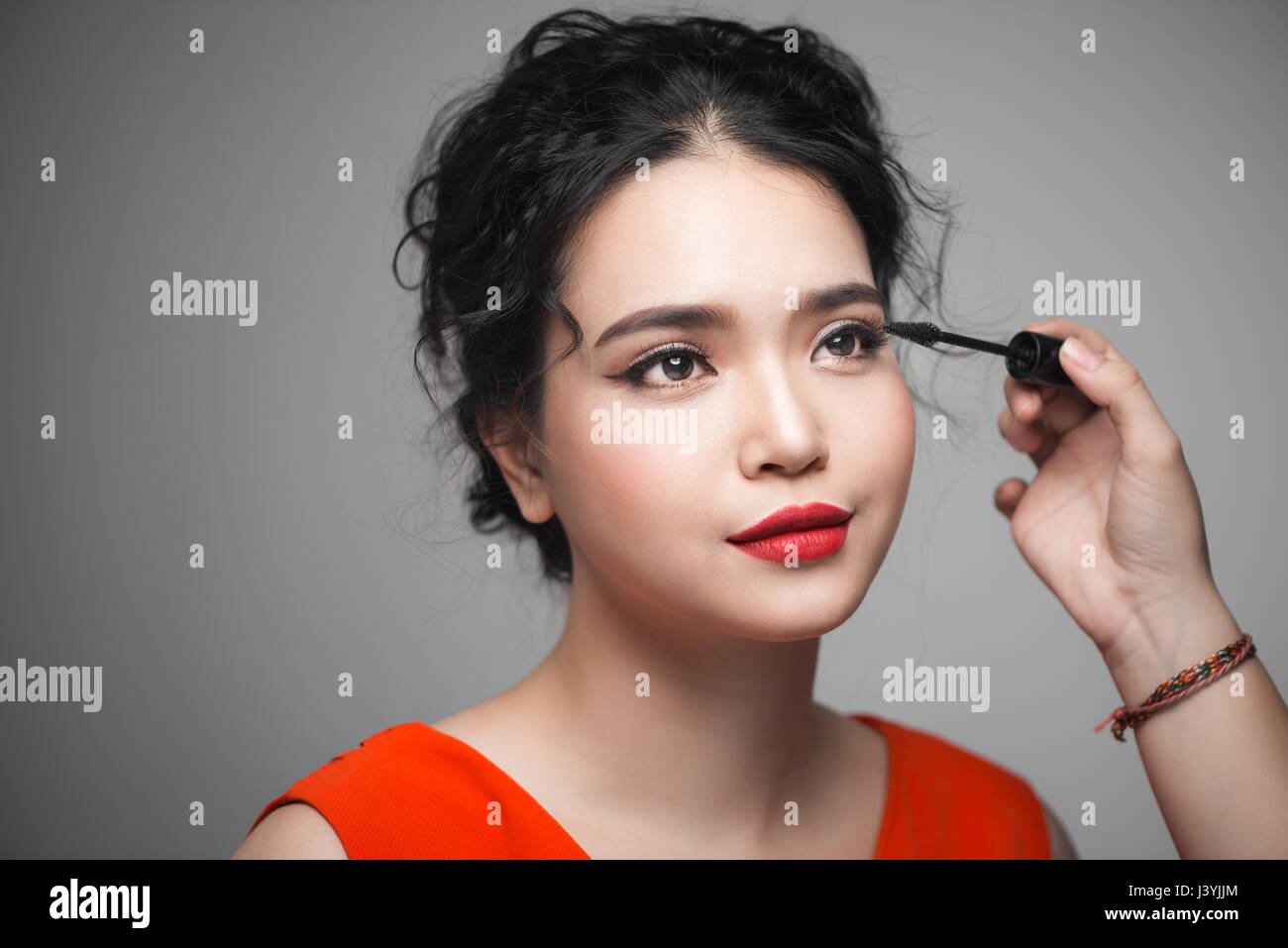 Beautiful young asian woman doing makeup using mascara on her eyelashes ...