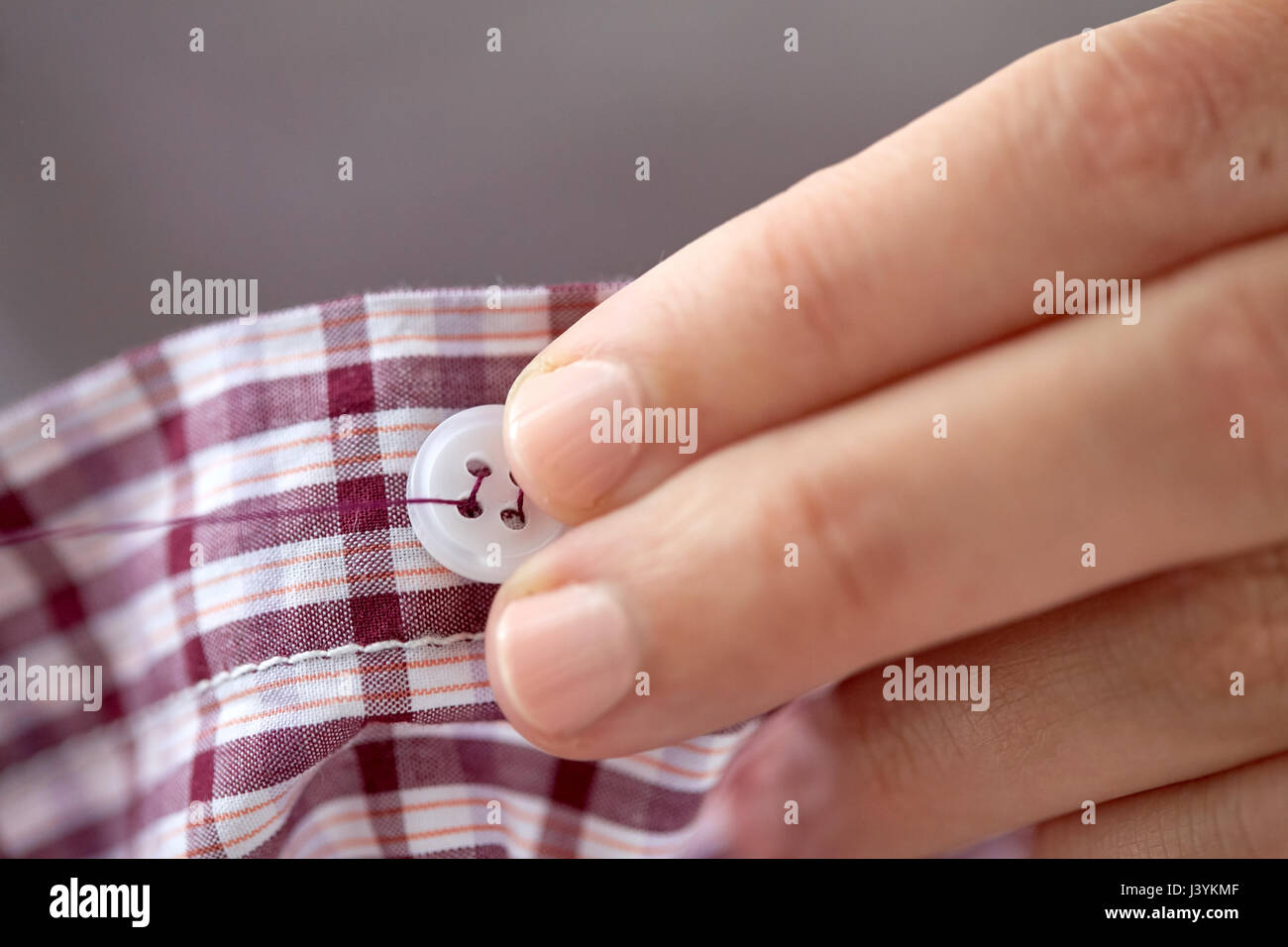 woman with needle stitching on button to shirt Stock Photo - Alamy