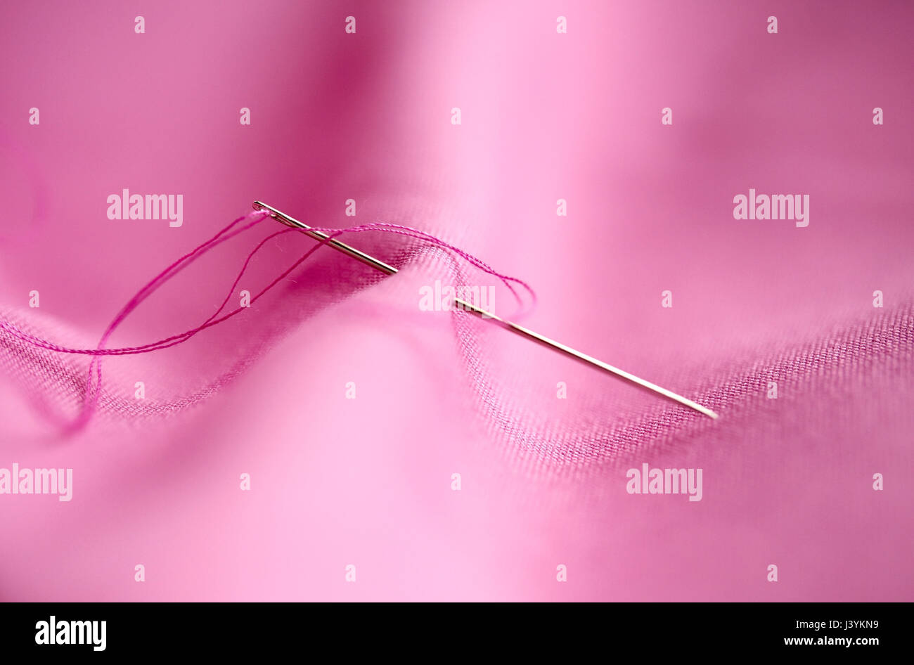 sewing needle with thread stuck into pink fabric Stock Photo - Alamy