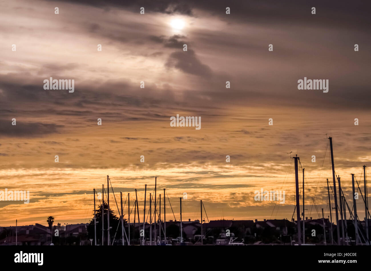Silhouettes of boats on marina during cloudy yellow sunset in Oxnard ...