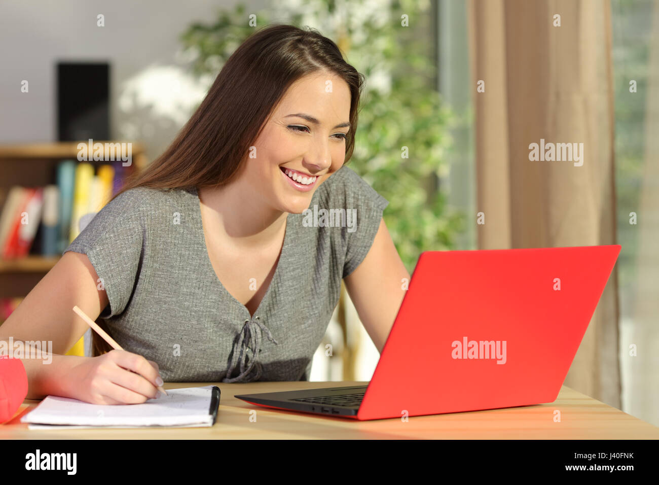 Student taking notes and learning on line with a red laptop sitting in ...