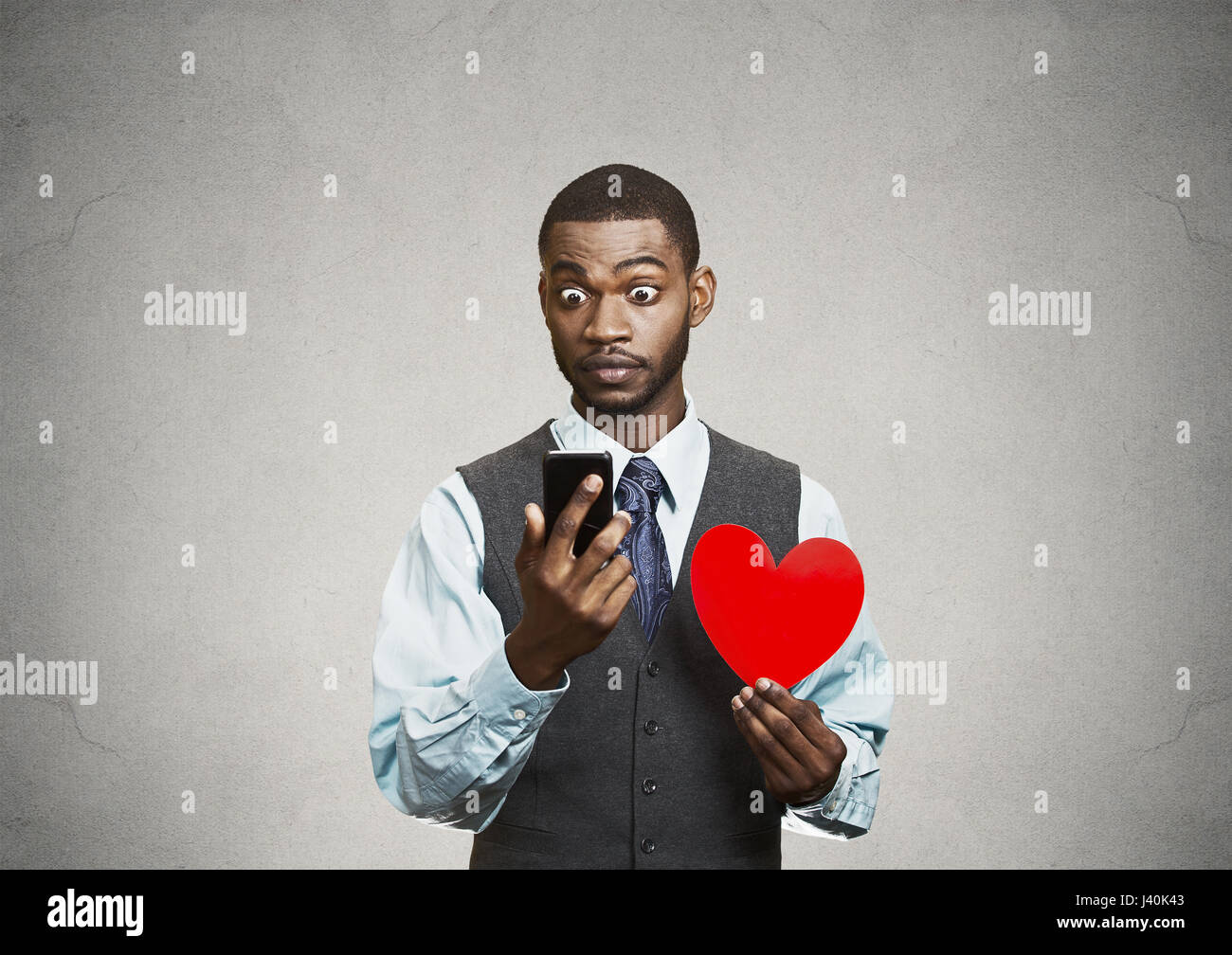 Closeup portrait puzzled young man reading breaking news on smart phone ...