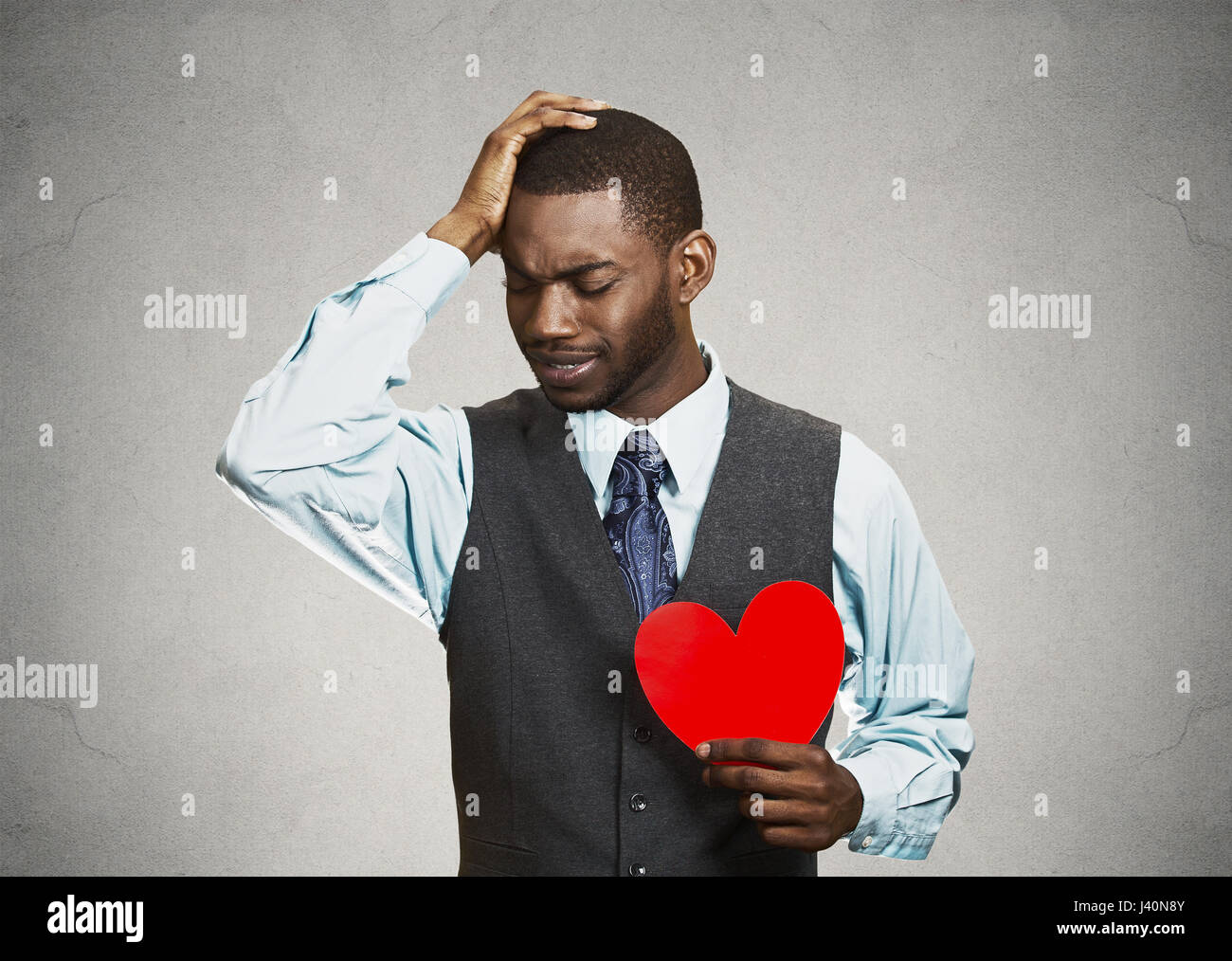 Closeup portrait young sad confused corporate man, holding red heart in ...
