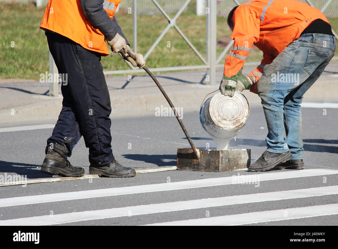 Workers apply a road marking to the pedestrian crossing zebra-stripe ...