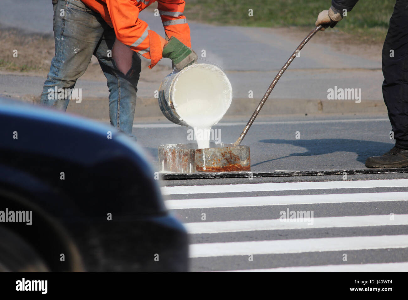 Workers apply a road marking to the pedestrian crossing zebra-stripe ...