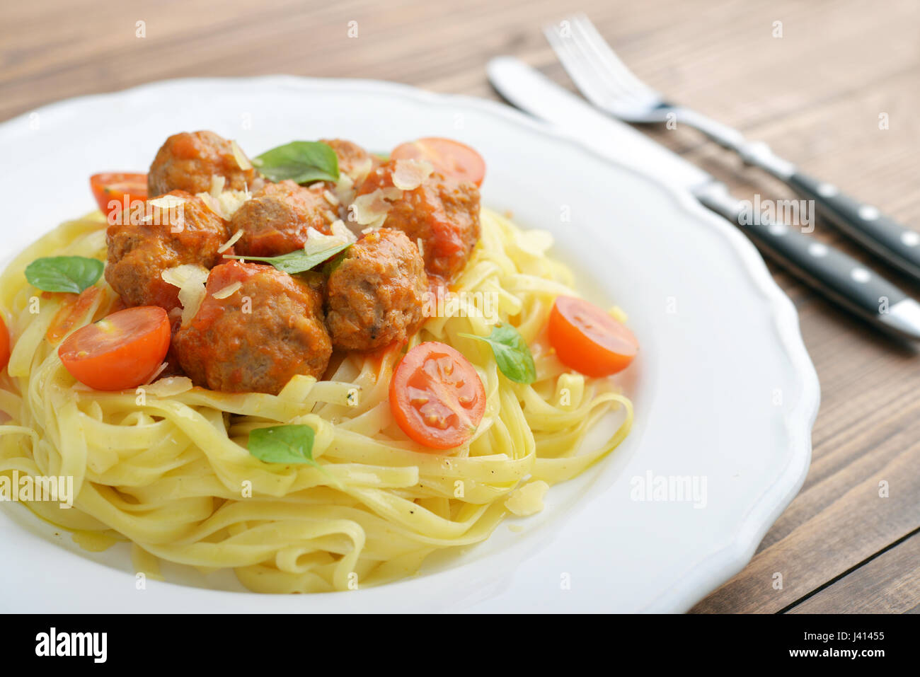 Tagliatelle pasta with meatballs and tomato sauce on plate over wooden ...