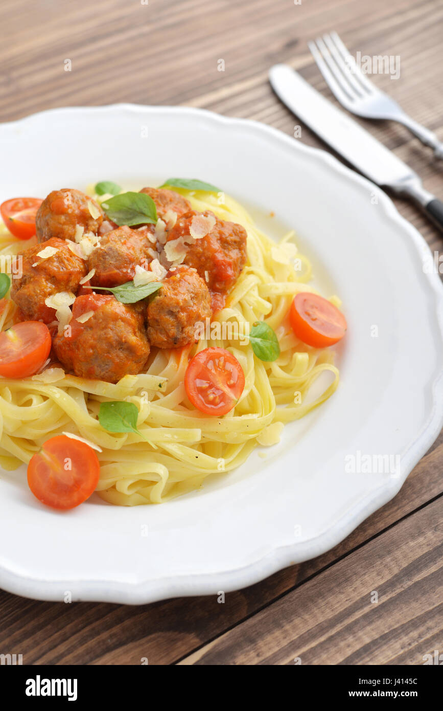 Tagliatelle pasta with meatballs and tomato sauce on plate over wooden ...