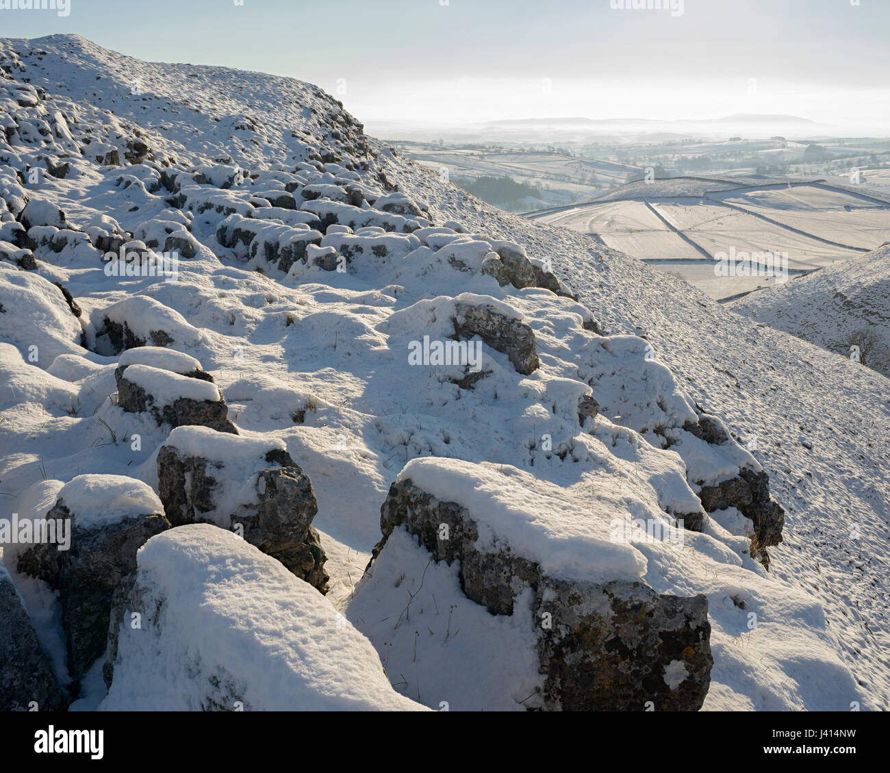 Sunlit snow on limestone pavement above Malham, Yorkshire Dales. View ...