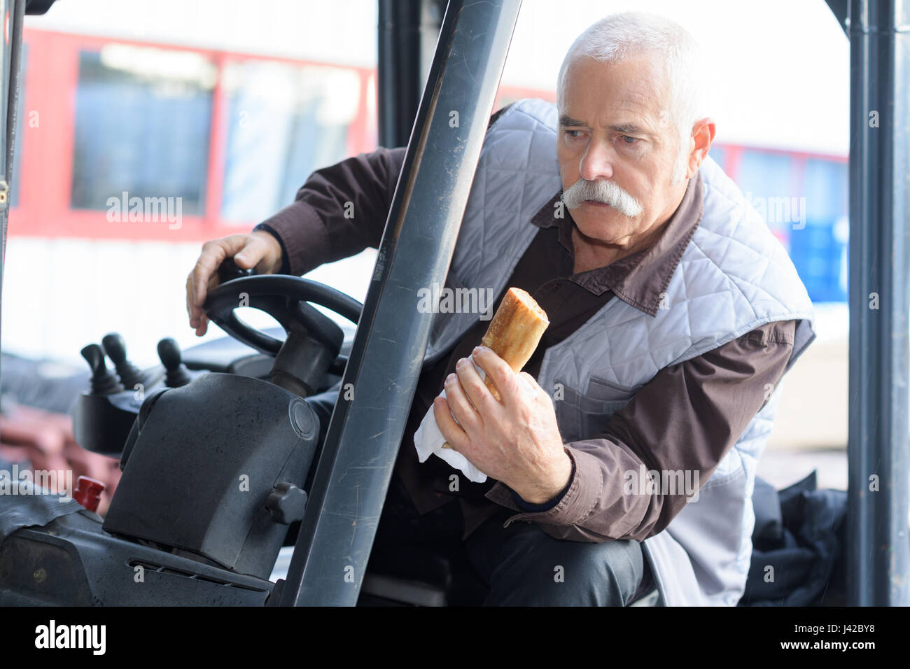 Man manoeuvering a fork lift truck while holding a sandwich Stock Photo ...