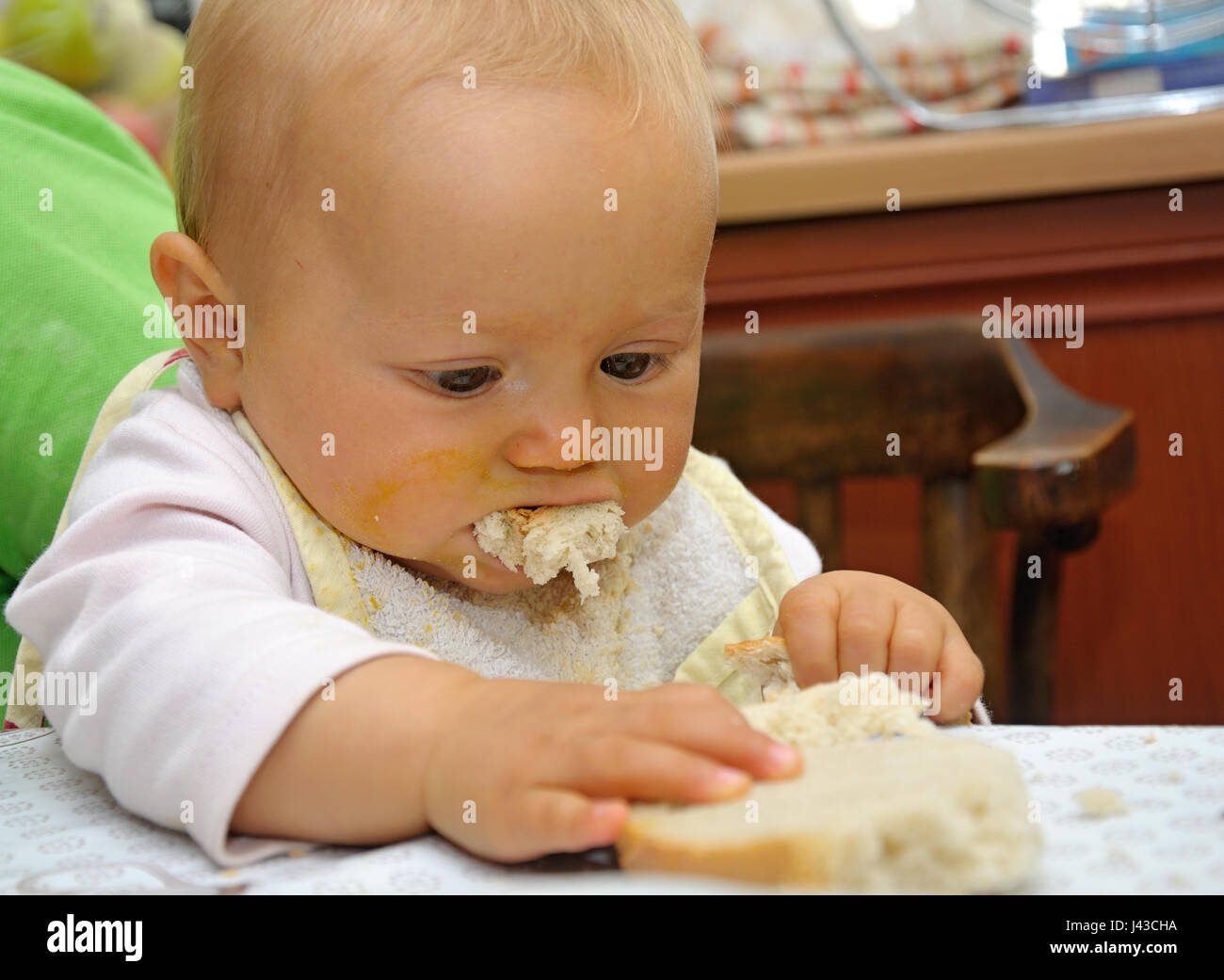 smiling baby eating food alone on kitchen Stock Photo - Alamy
