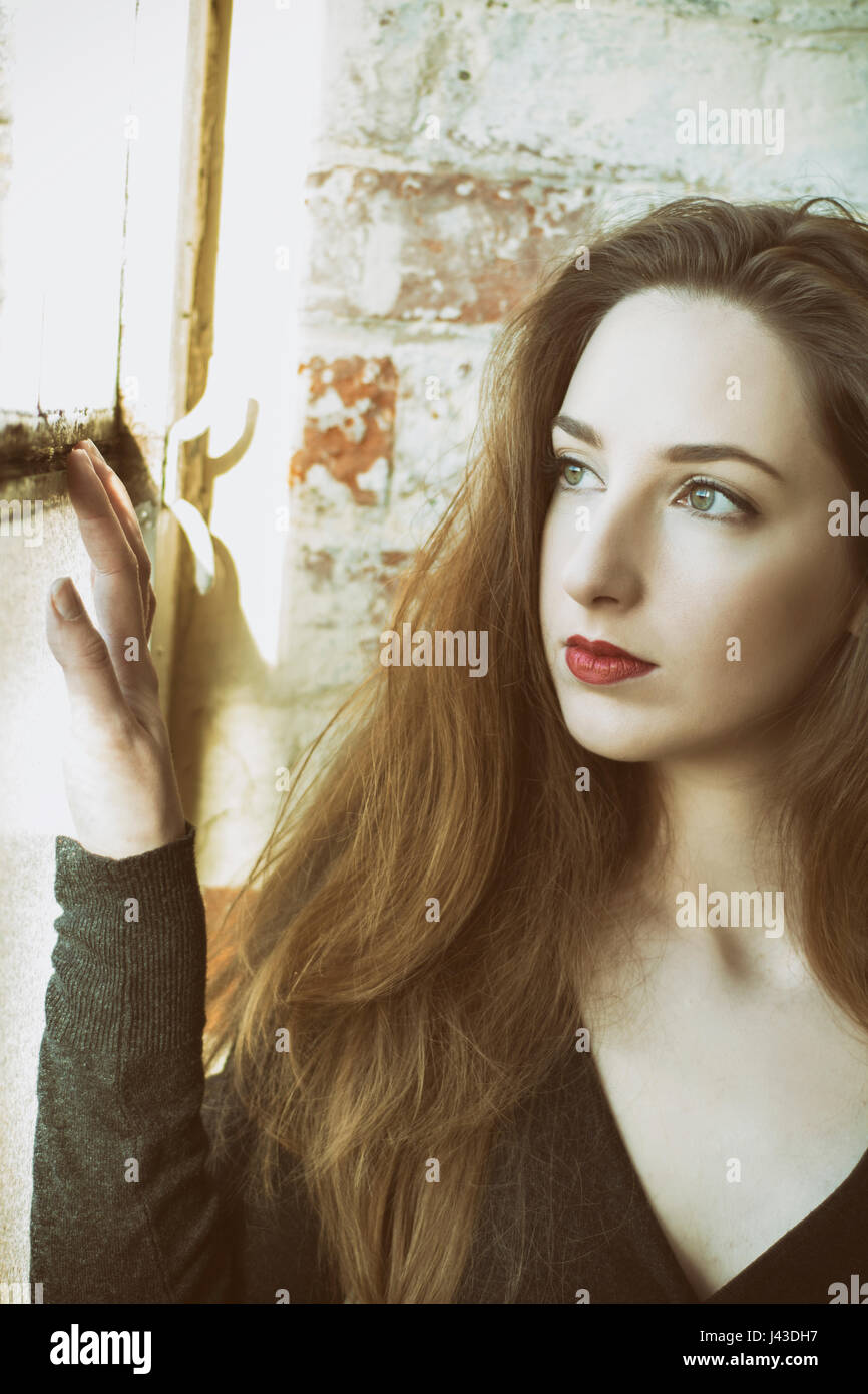 Beautiful young woman looking out of the window hand touching the glass ...
