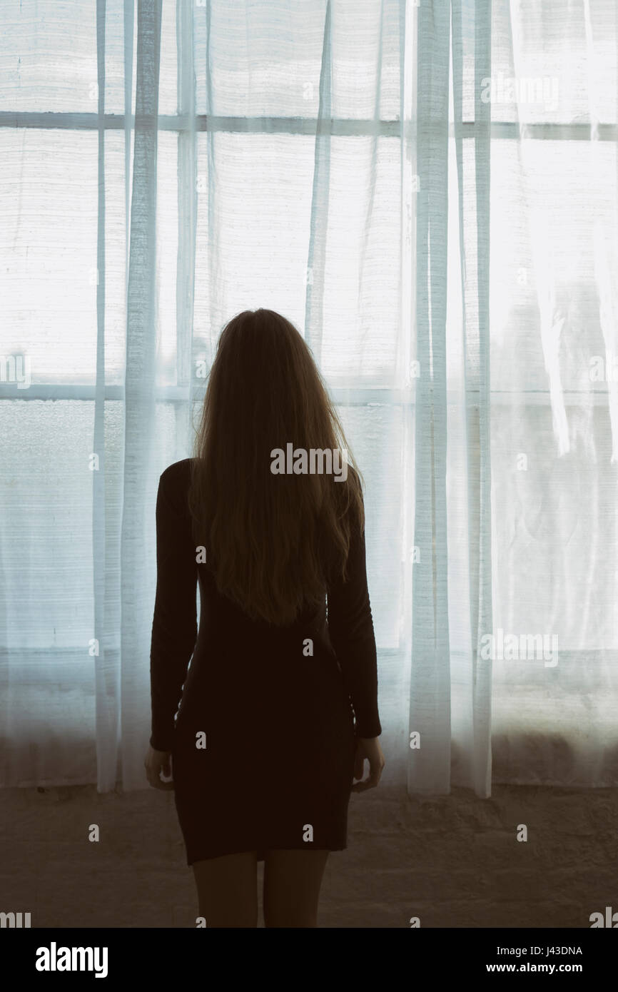 Rear view of a young woman standing by the window Stock Photo - Alamy