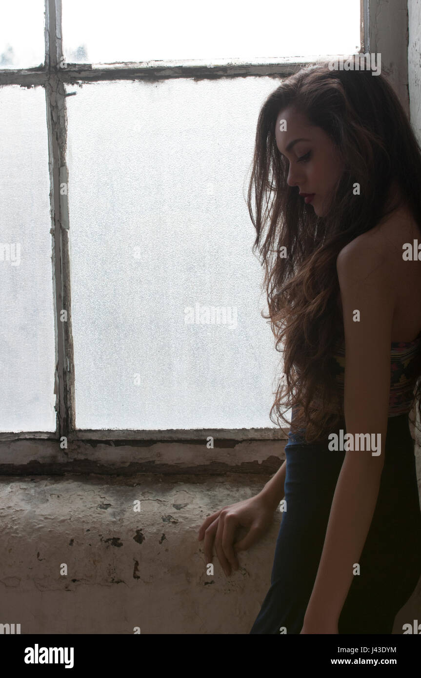 Sad young woman standing by the window Stock Photo - Alamy