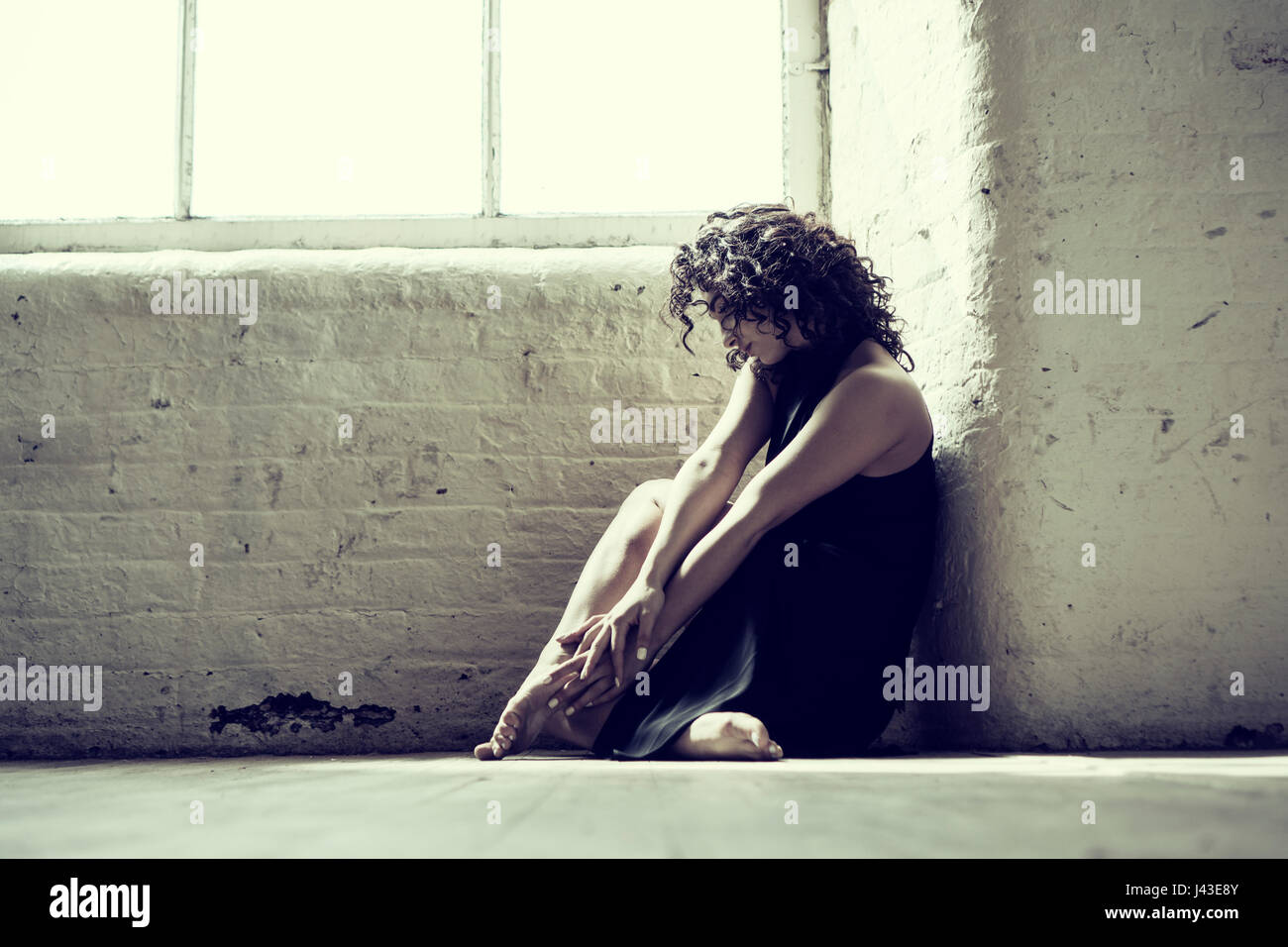 Sad young woman wearing a short black dress sitting on the floor by the ...