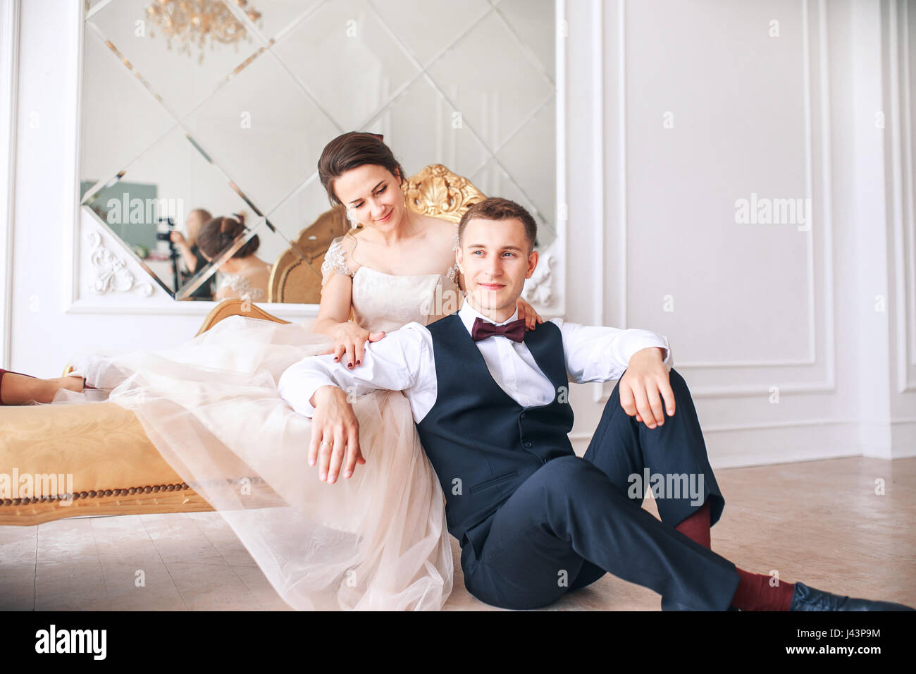 Bride in beautiful dress and groom in black suit sitting on sofa ...