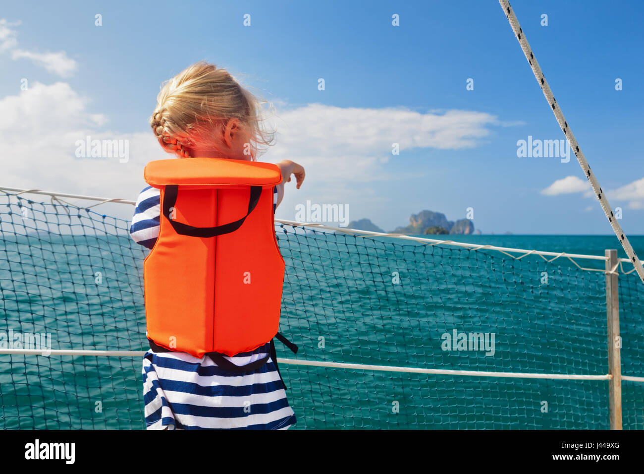 Happy little baby in life jacket on board of sailing boat watching ...