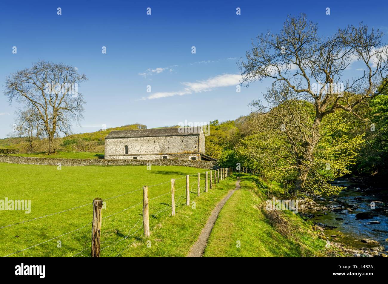 An isolated barn set in green English countryside by a path running ...