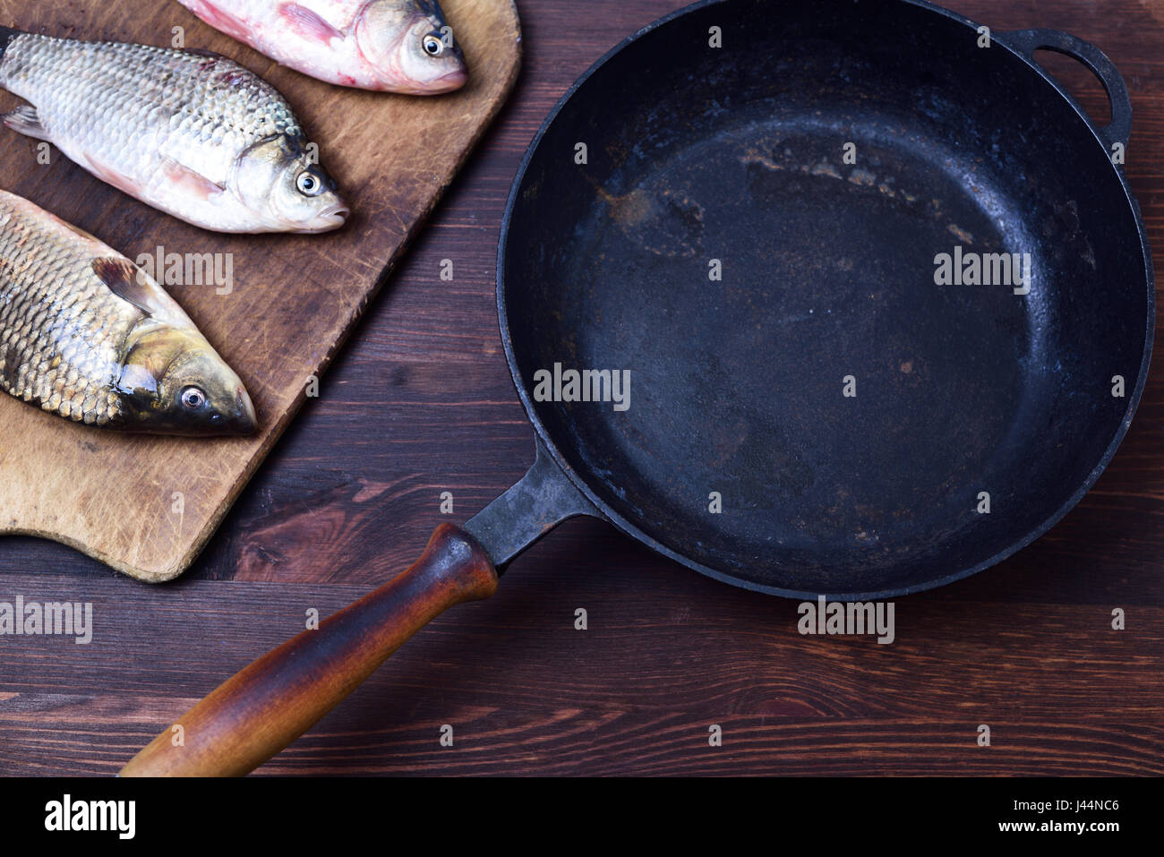 Three fresh carp fish, next to a black cast-iron frying pan, top view ...