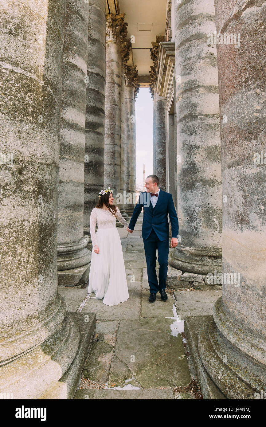 Young newlywed couple posing between rows of antique building columns ...