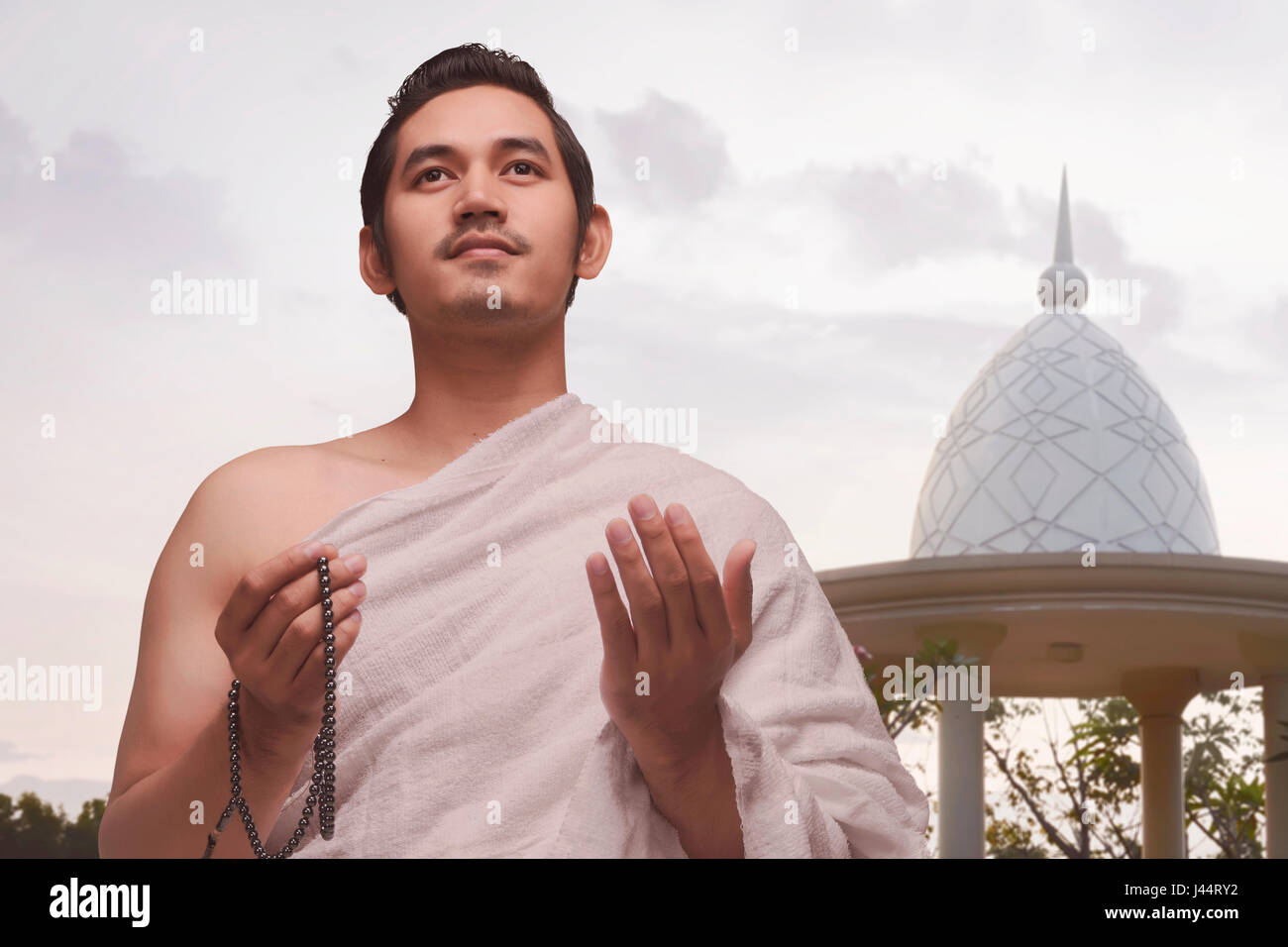 Smiling asian muslim man with ihram clothes holding prayer beads over ...
