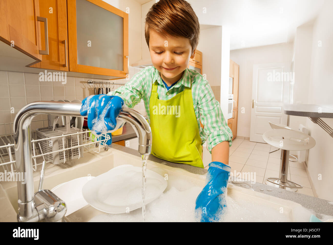 Happy kid boy rinsing dishes in the sink Stock Photo - Alamy