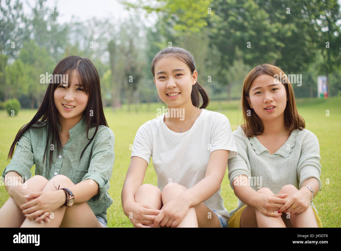 Three girls in the outdoor lawn sit Stock Photo - Alamy