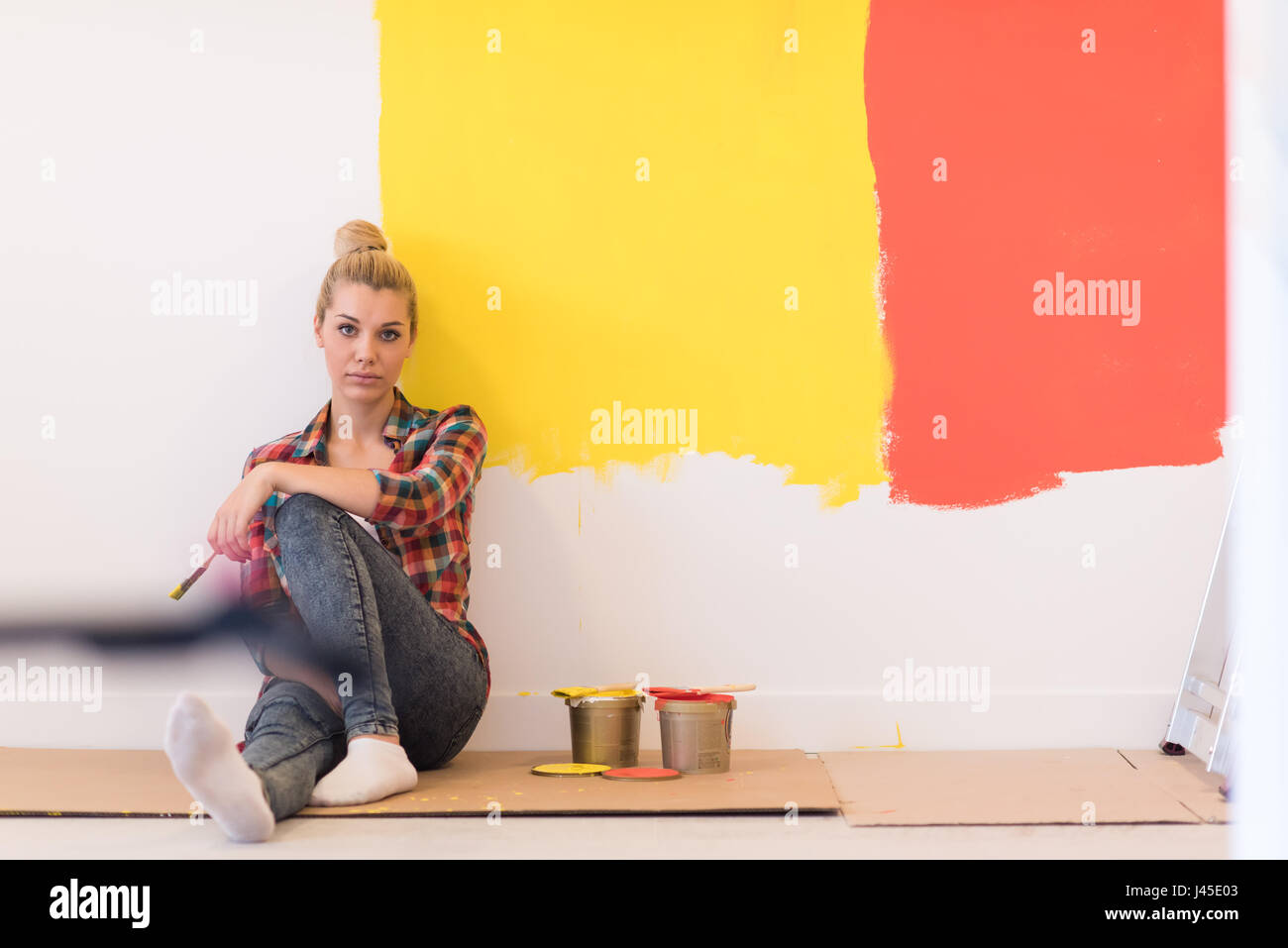 Portrait of a beautiful young female painter sitting on floor near wall ...