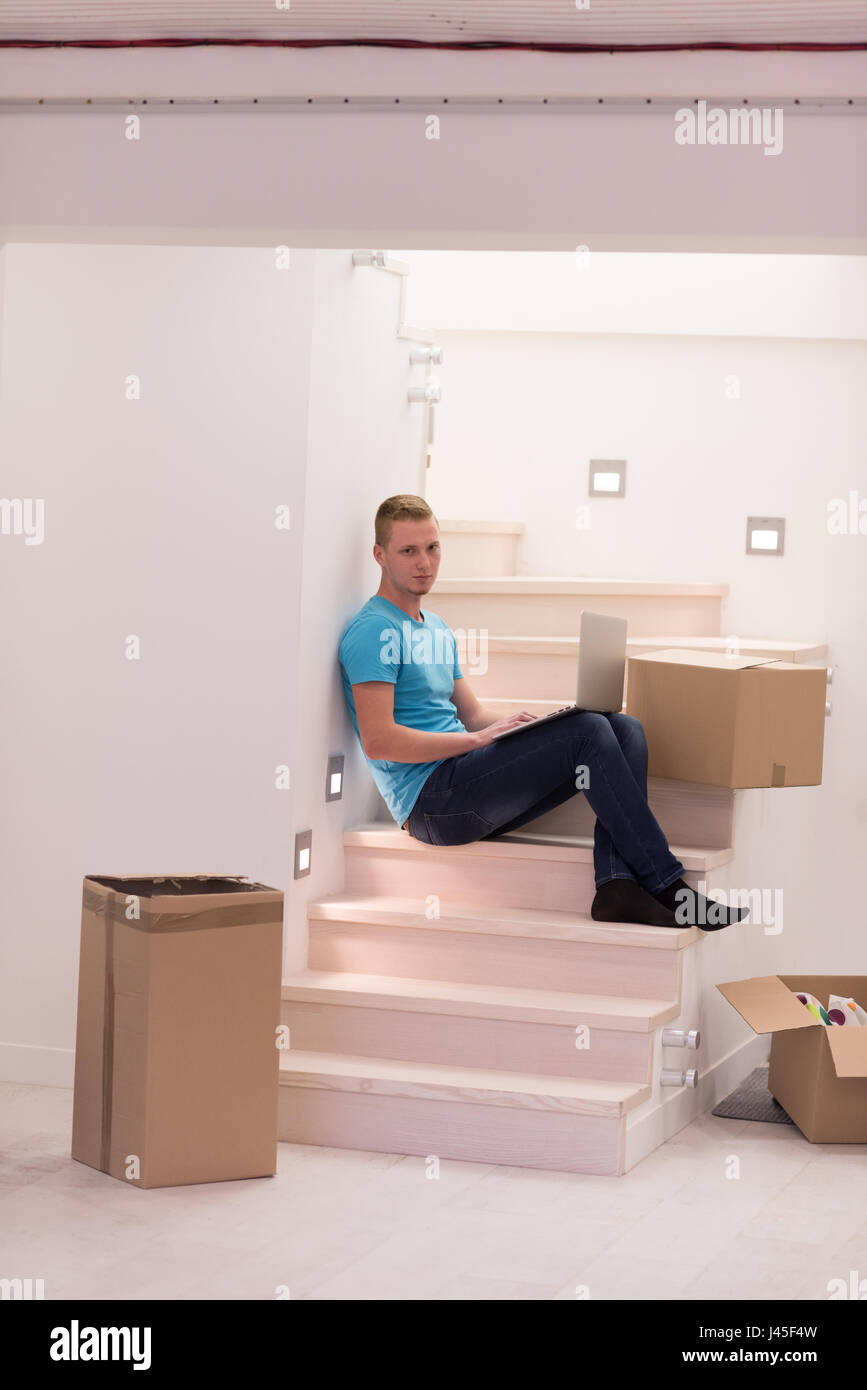 Happy young man sitting in stairway at home, using laptop computer with ...